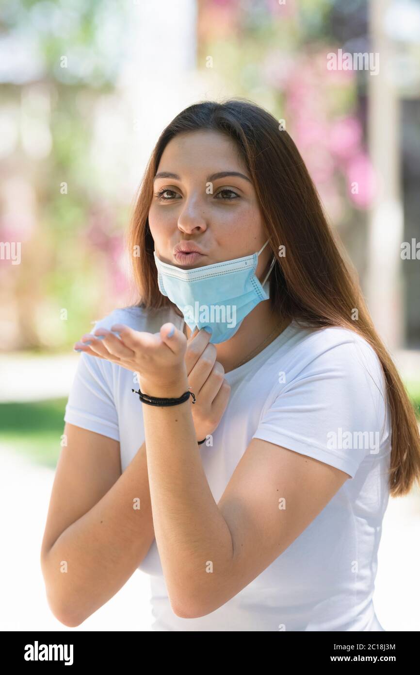 Young beautiful woman pulling down her surgical mask and blowing a kiss ...