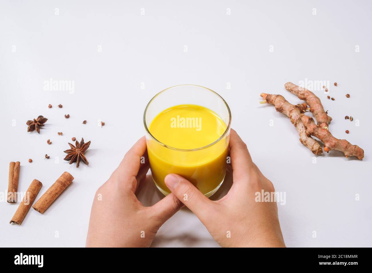 Hands holding glass of golden milk turmeric curcumin latte yellow drink ...