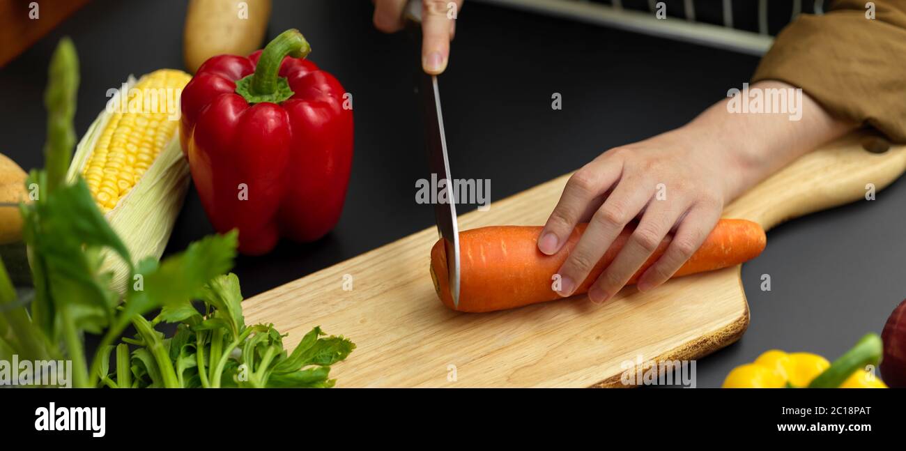Close up view of female cook slicing fresh carrot on chopping block at ...