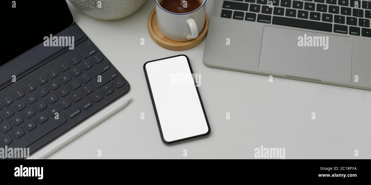 Top view of blank screen smartphone on white office desk with laptop ...
