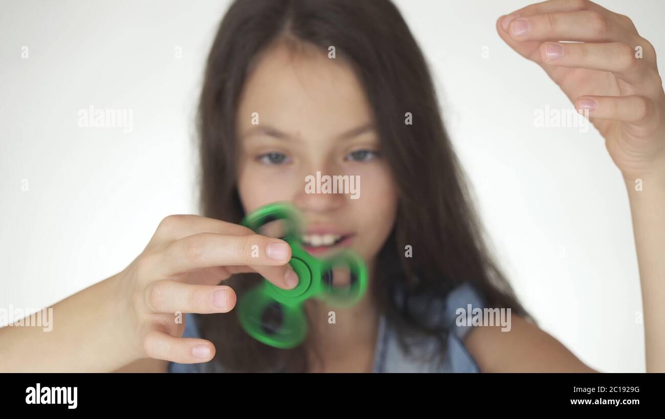 Beautiful cheerful teen girl playing with green fidget spinner on white ...