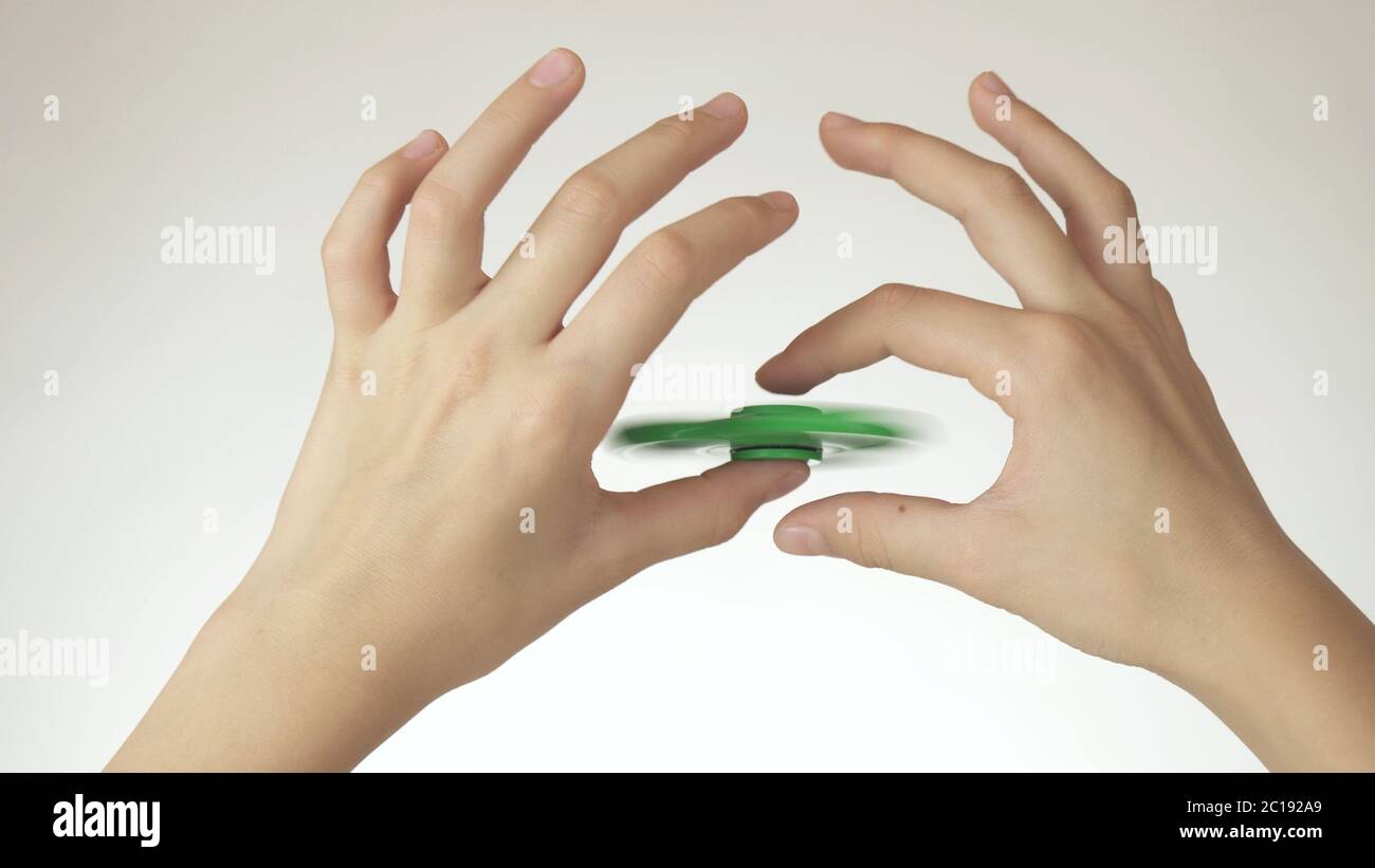 Hands of a teenage girl spin a green fidget spinner on white background ...