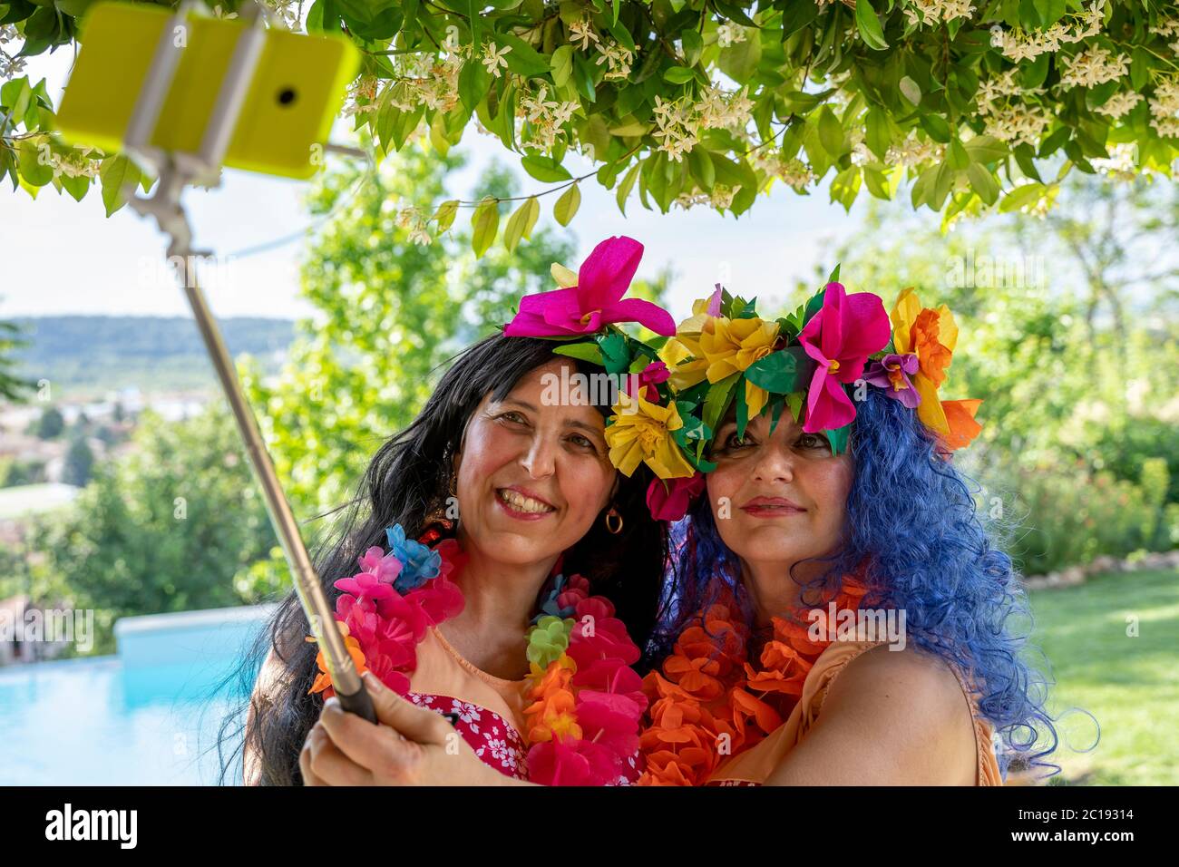 two smiling female friends dressed in Hawaiian costumes take a selfie ...