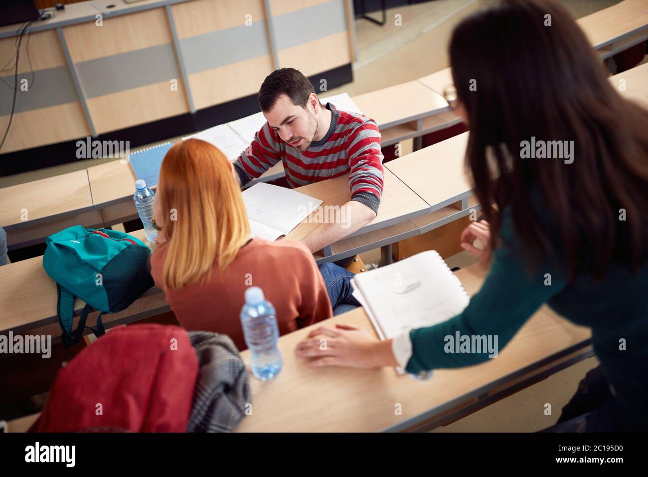 Young freshman students talking and comparing notes in amphitheater ...