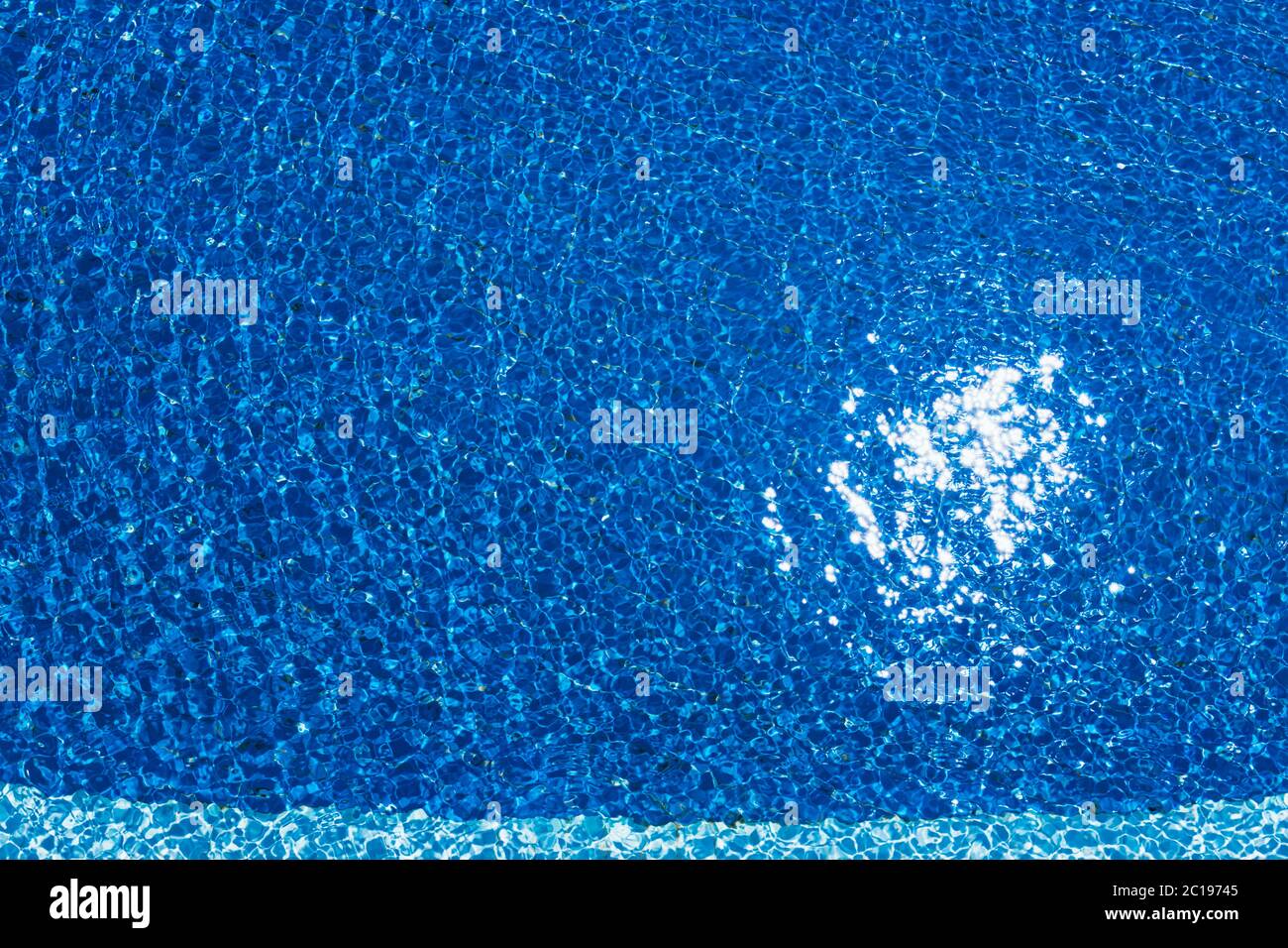 Swimming pool, blue clear water in the outdoor pool, with sun flare on ...