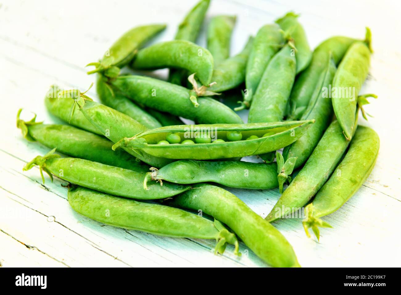 Fresh peas in the pod with one opened on the top of the pile to display ...