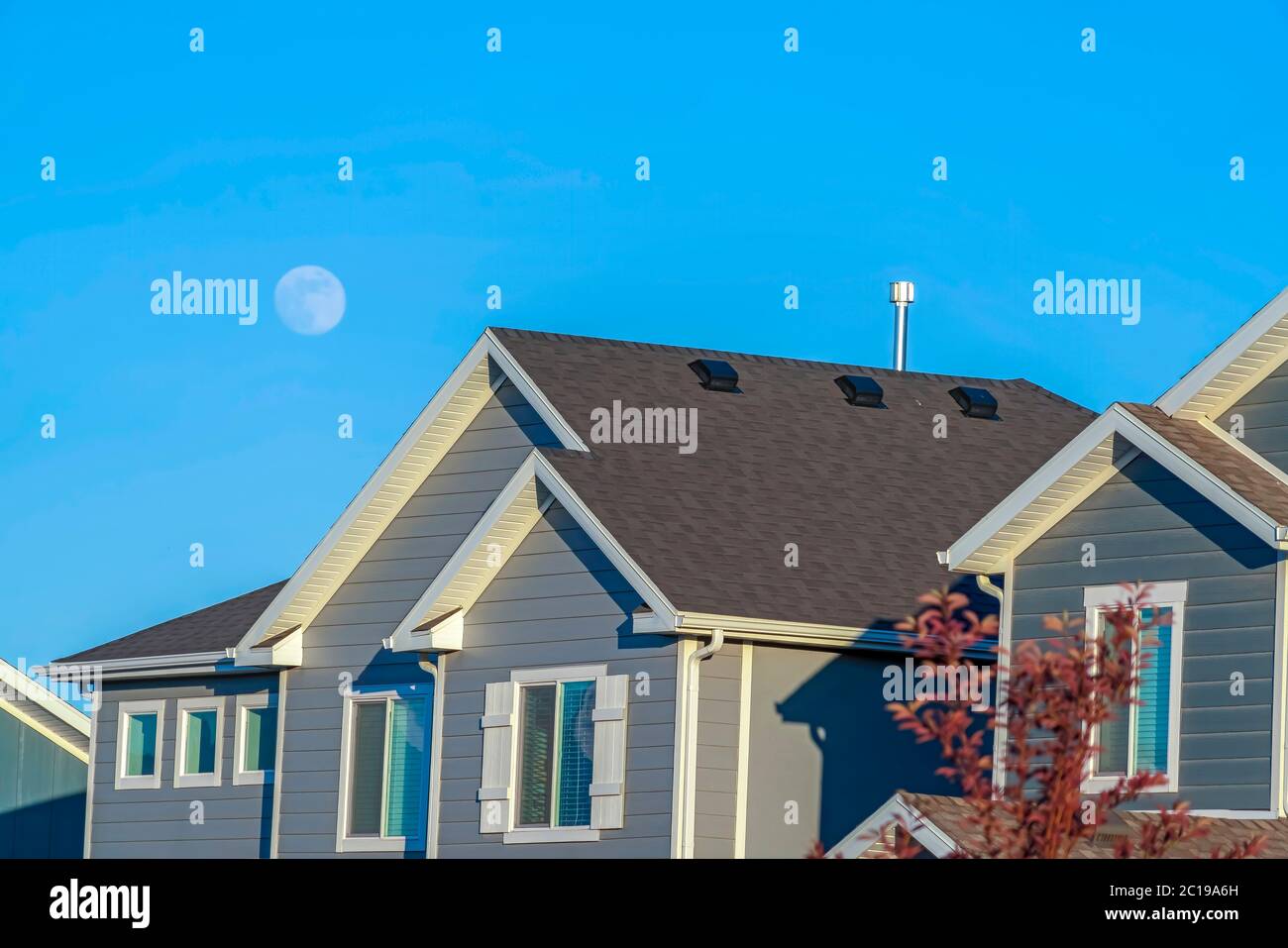 Sunlit home with dark pitched roof over horizontal gray wall siding and ...