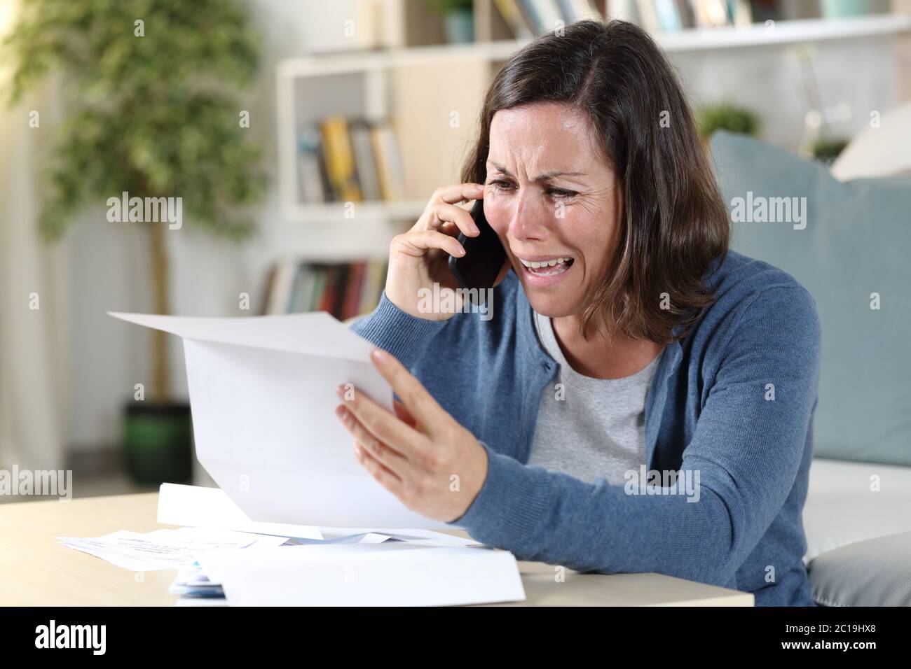 Sad adult woman crying calling on smart phone with letter sitting on ...