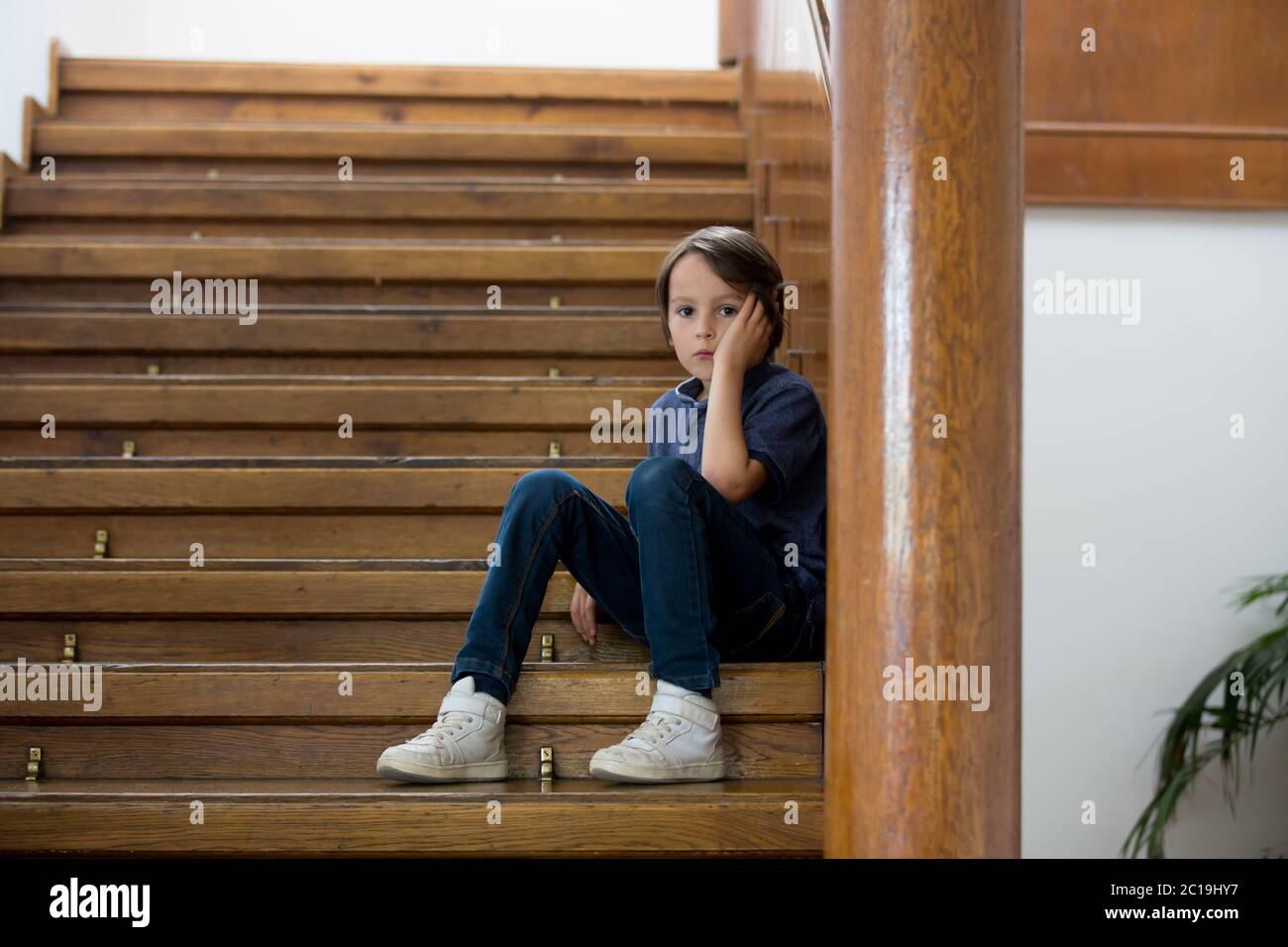 Sad child, sitting on a staircase in a big house, concept for bullying ...