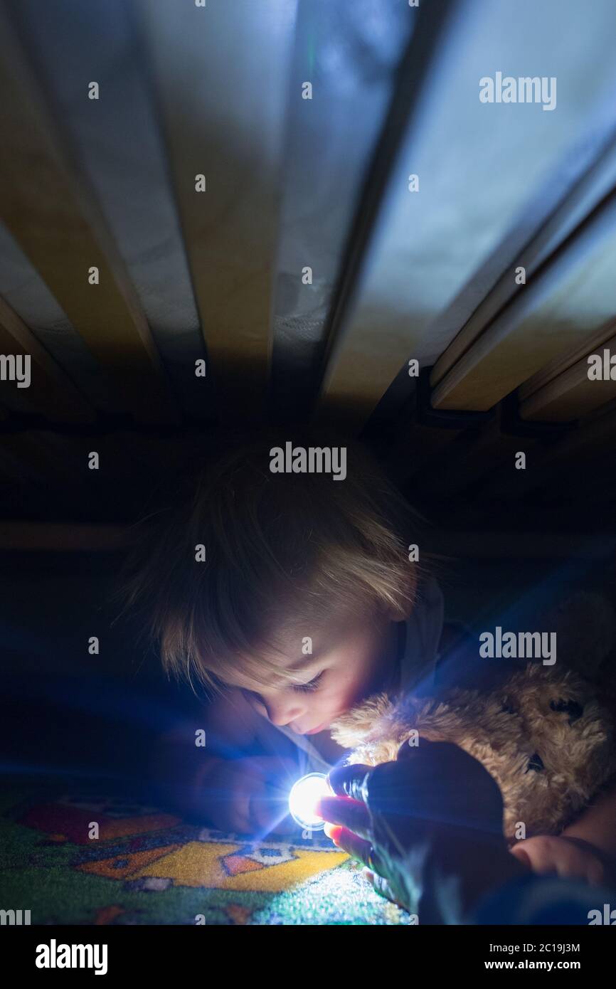 Little child, hiding under the bed, hugging teddy bear and holding ...