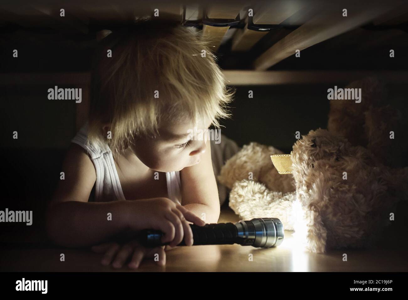 Little child, hiding under the bed, hugging teddy bear and holding ...