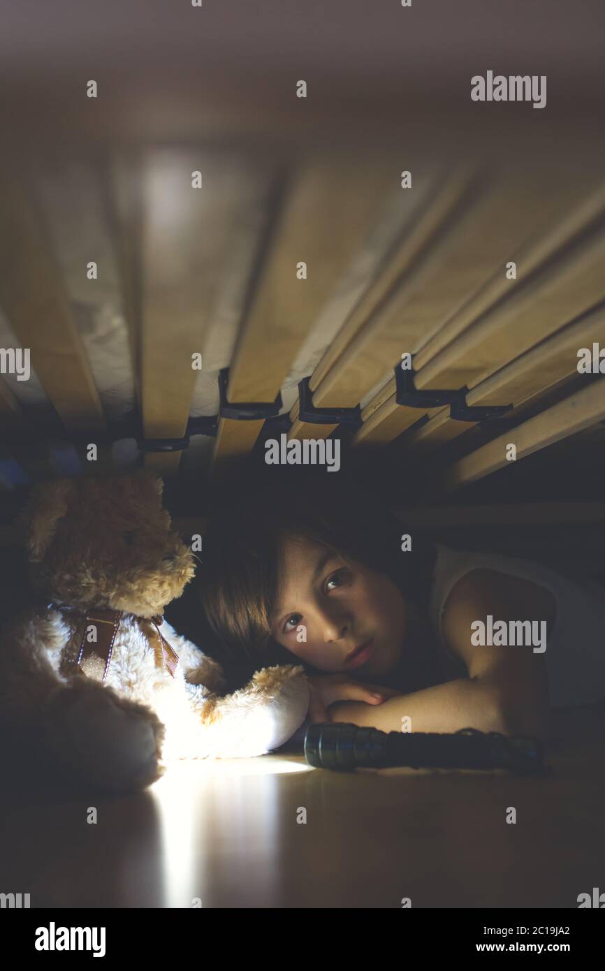Little child, hiding under the bed, hugging teddy bear and holding ...