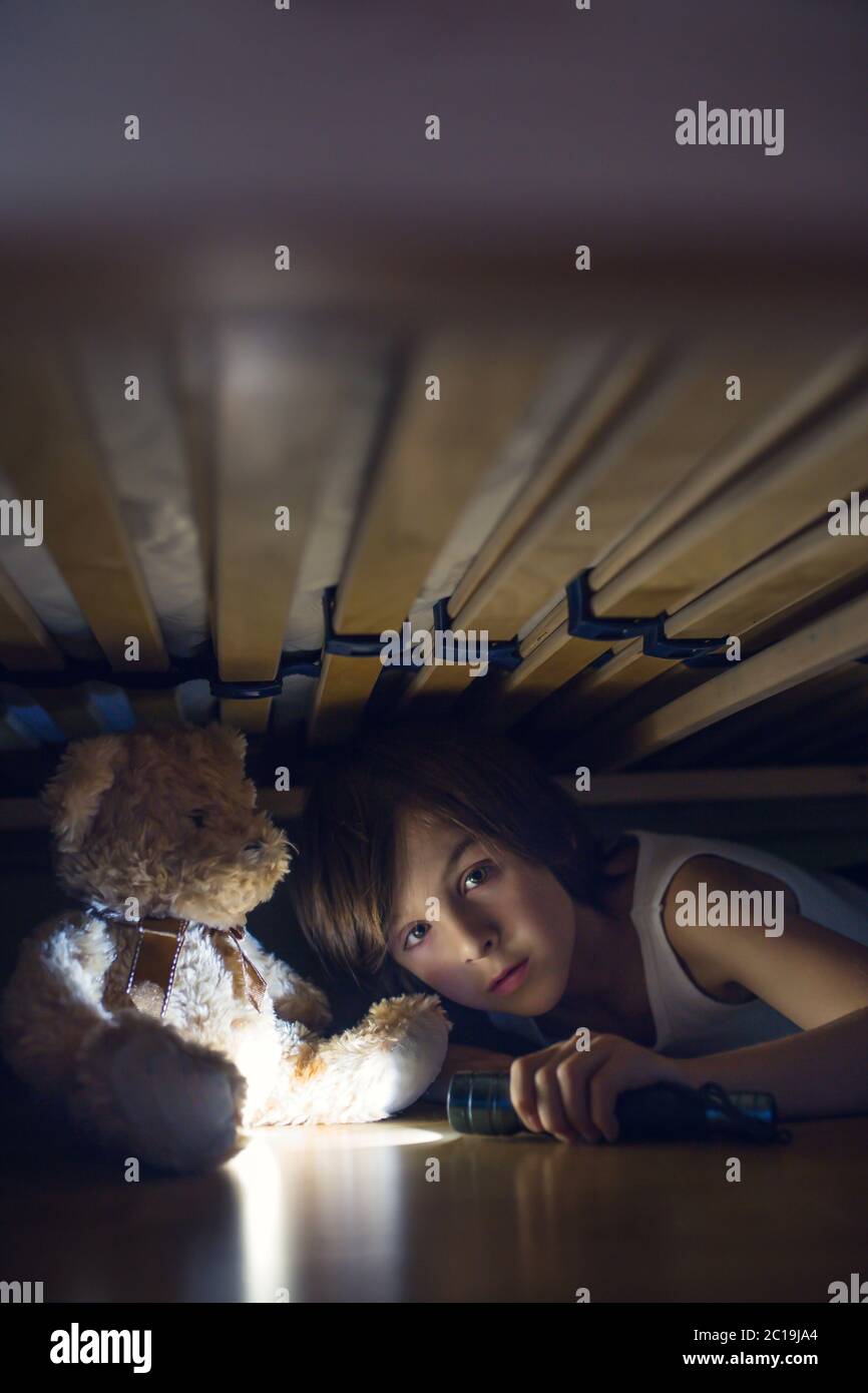 Little child, hiding under the bed, hugging teddy bear and holding ...