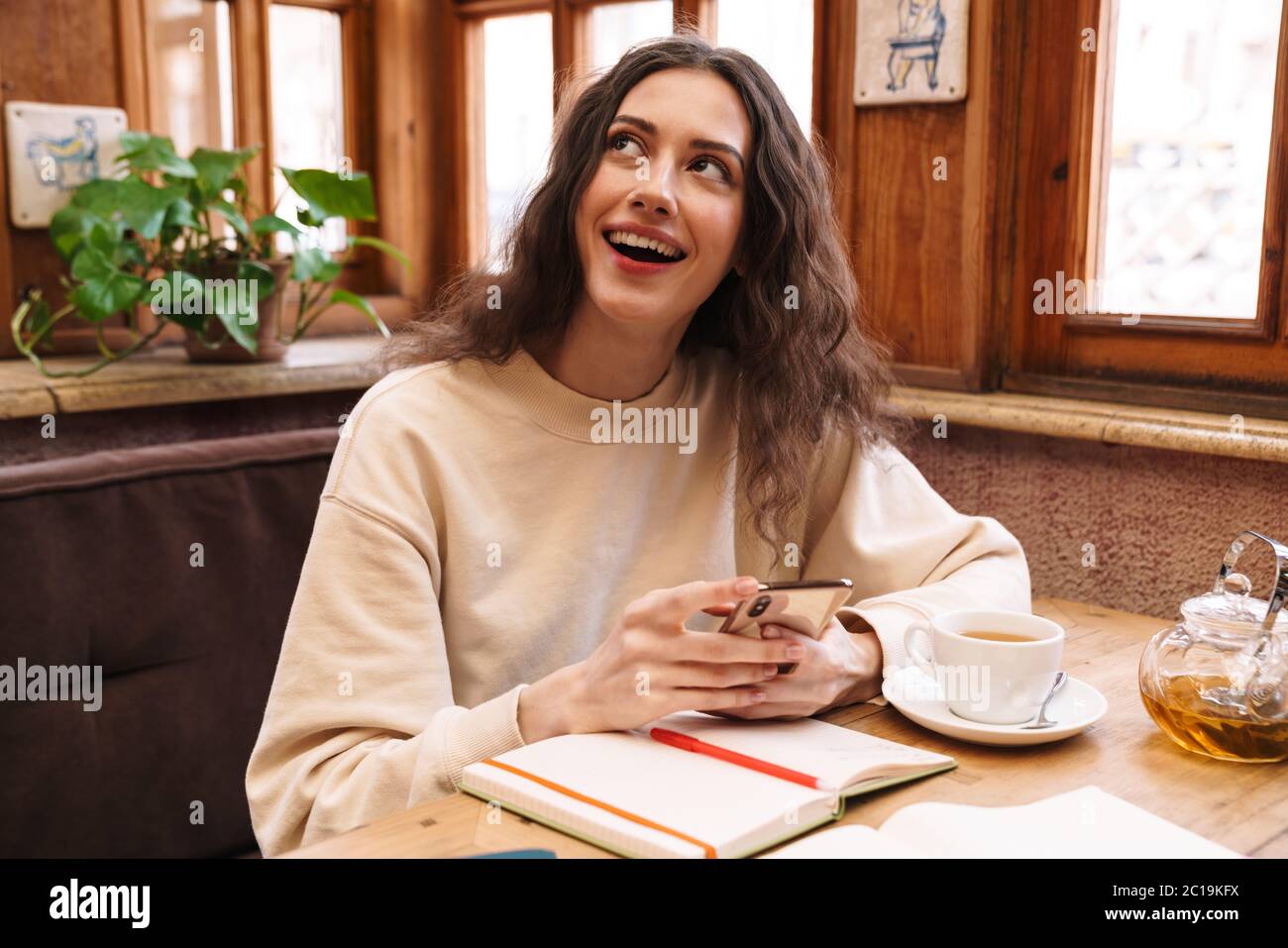 Image of joyful student woman doing homework and using cellphone while ...