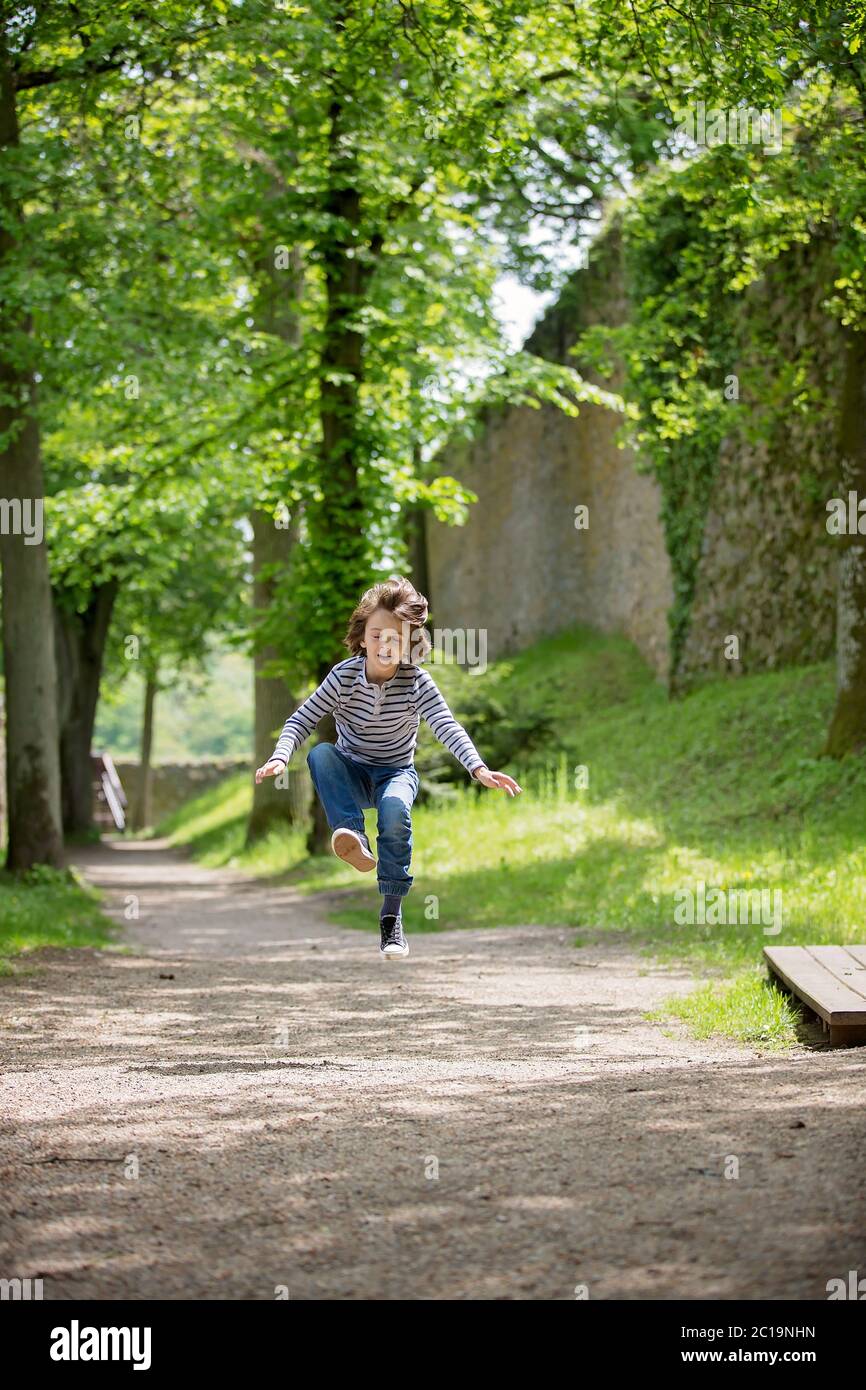 Happy Child, boy, running and jumpring on path in park with trees and ...