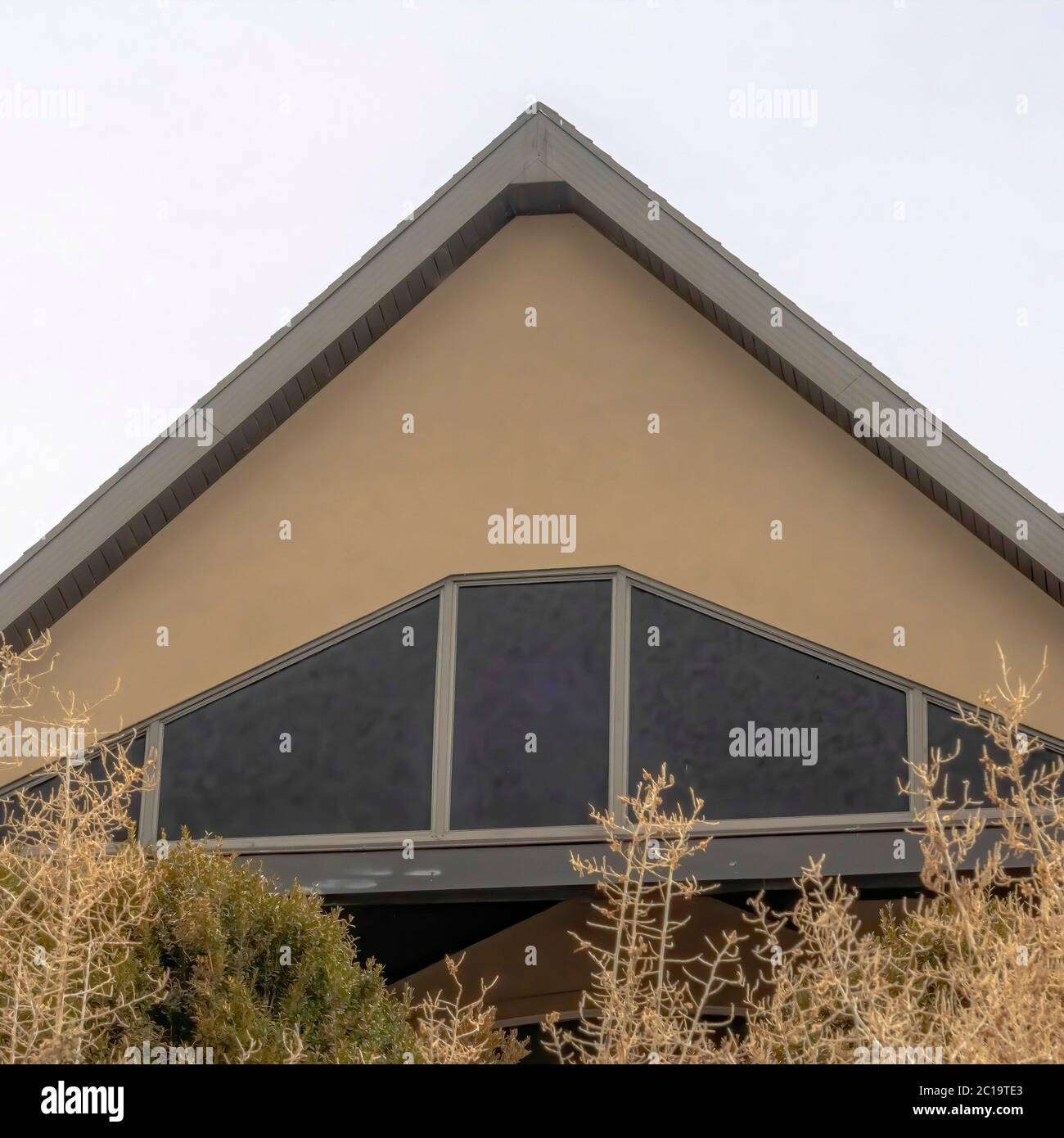 Square Home exterior with front gable roof at entrance viewed behind ...