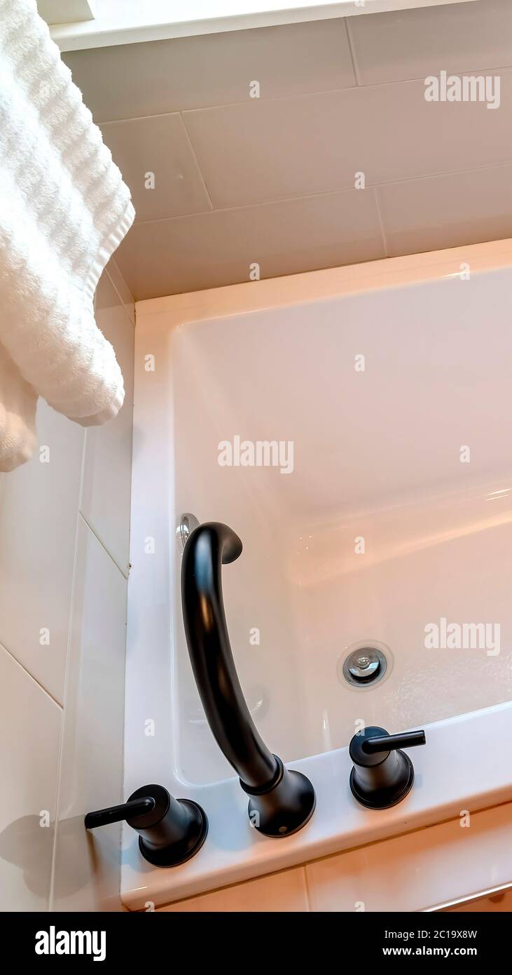 Vertical crop Rectangular bathtub with black faucet and handles against ...