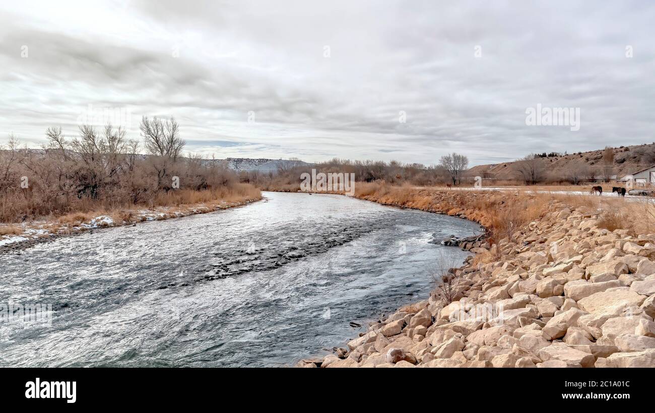 Panorama crop Glistening river with grassy and rocky banks along houses ...