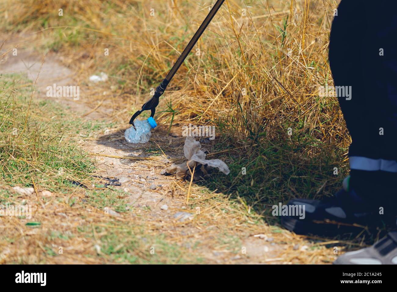 Closeup of hand and waste grabber picking up drinking plastic bottle ...
