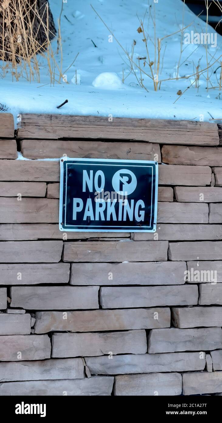 Vertical No Parking sign on a stone brick retaining wall topped with ...