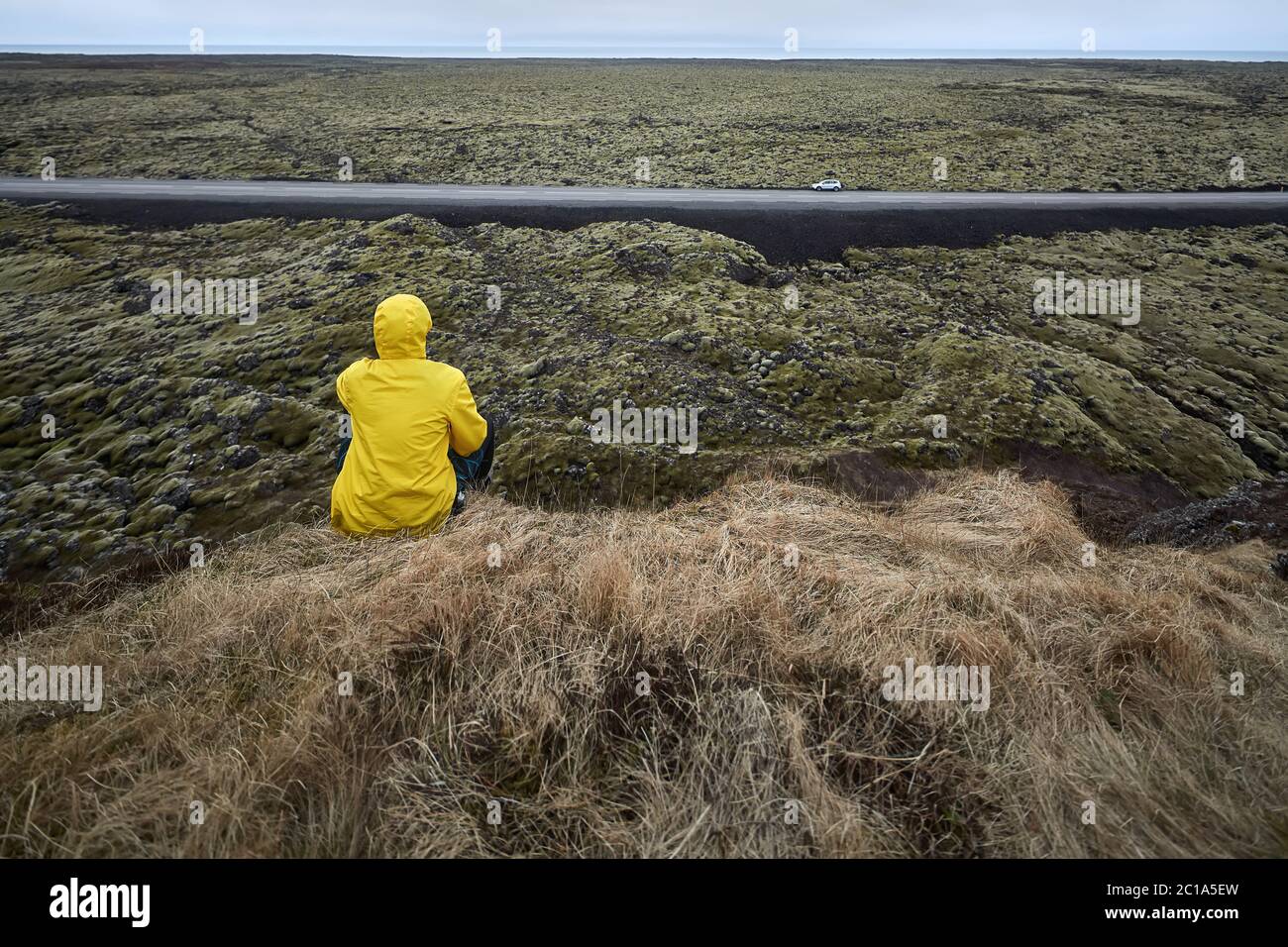 Man sits on cliff opposite country roadway Stock Photo - Alamy