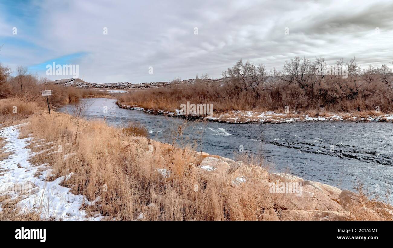 Panorama River with flowing water along grassy and rocky banks dusted ...