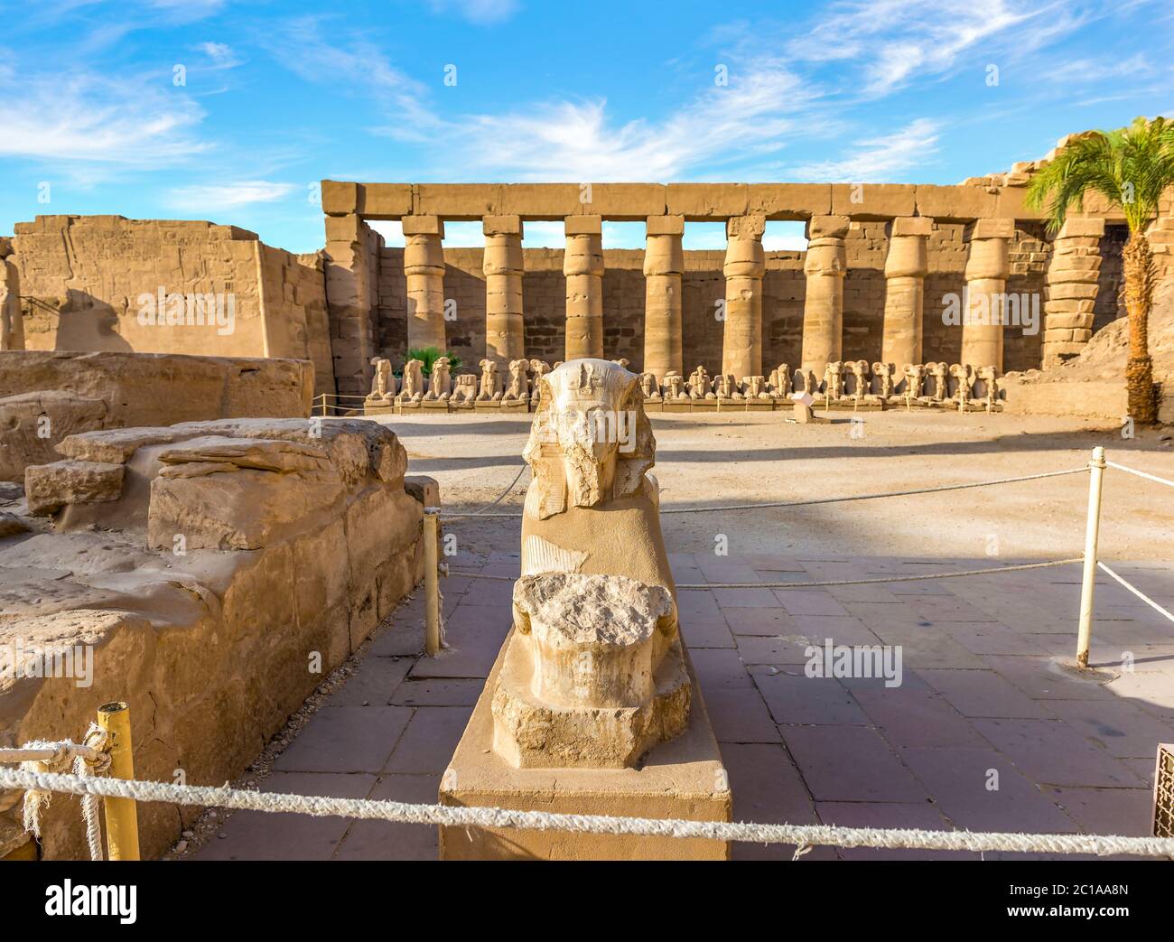 Ruined statue in Karnak Temple in front of colonnade with sphinxes ...