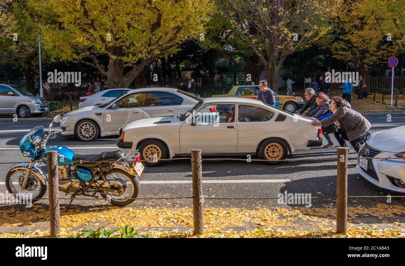 A group of people pushing a broken down car at Jingu Gaien Ginkgo ...