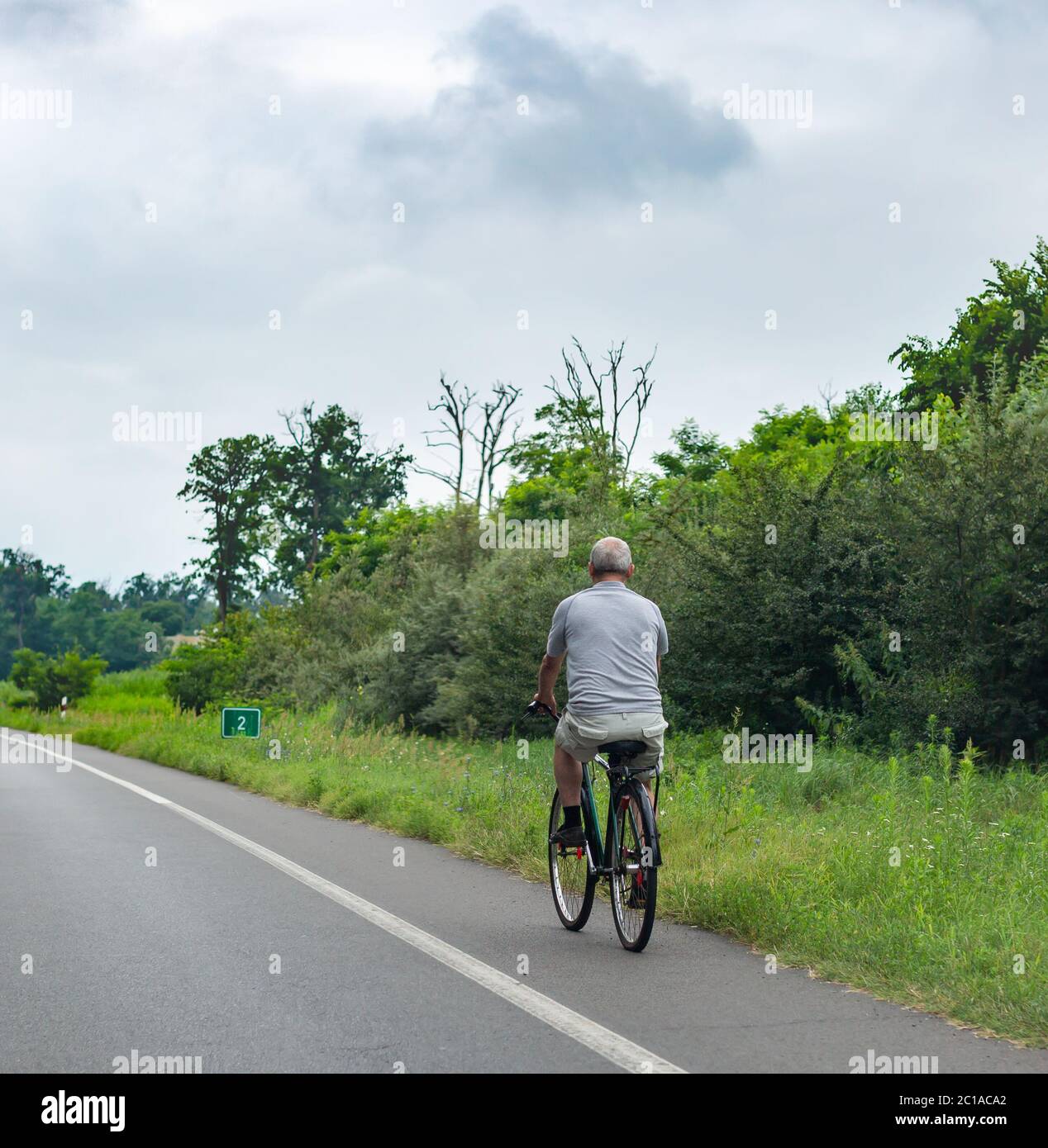 Gray haired man riding bicycle on bike lane on the edge of road Stock ...
