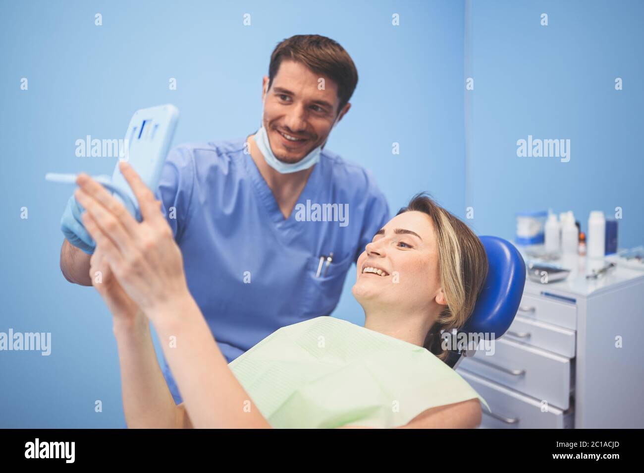 Dentist shows patient the results of treatment with a mirror, examinating teeth with dental ...