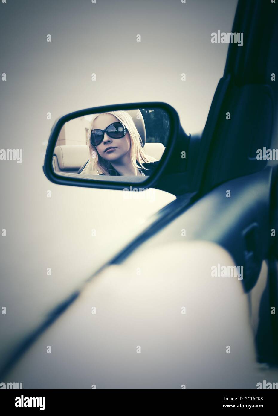 Blond woman in sunglasses looking in the car rear view mirror Stock ...