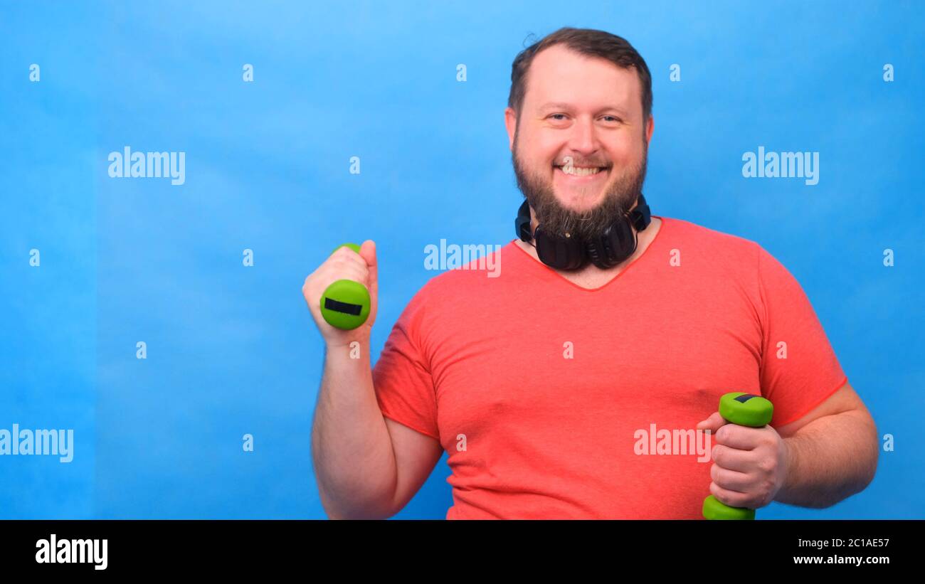 Funny fat man freaky in a wig and a pink t-shirt with dumbbells doing ...