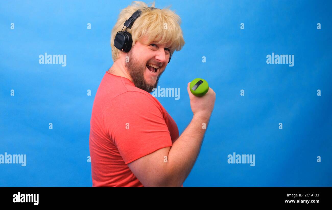 Funny fat man freaky in a wig and a pink t-shirt with dumbbells doing ...