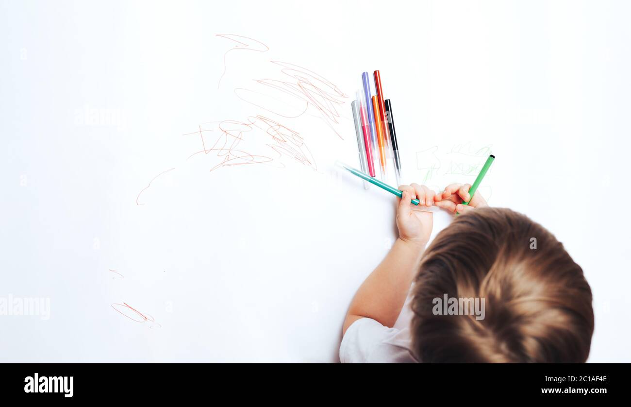 Little child draws on white paper with colored felt-tip pens, teaching ...