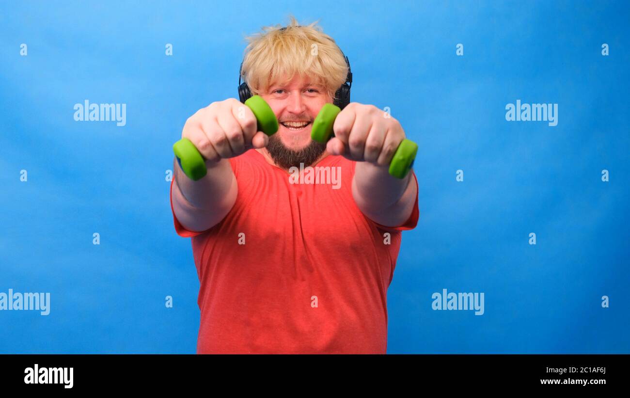 Funny fat man freaky in a wig and a pink t-shirt with dumbbells doing ...