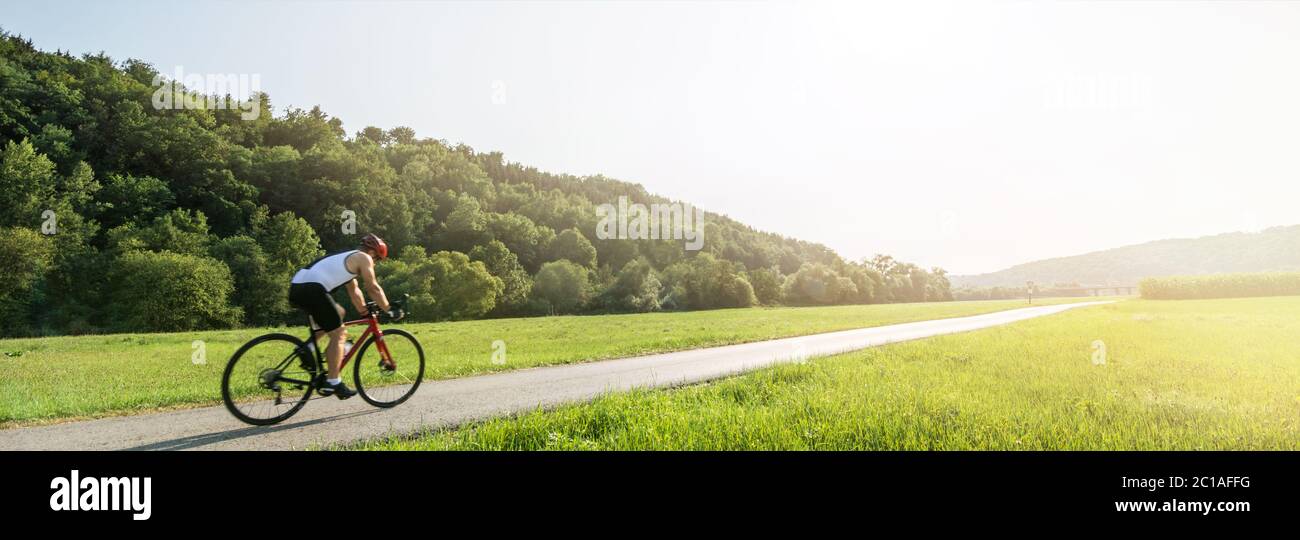 Panorama shot of cyclist on racing cycle in a rural landscape in summer ...