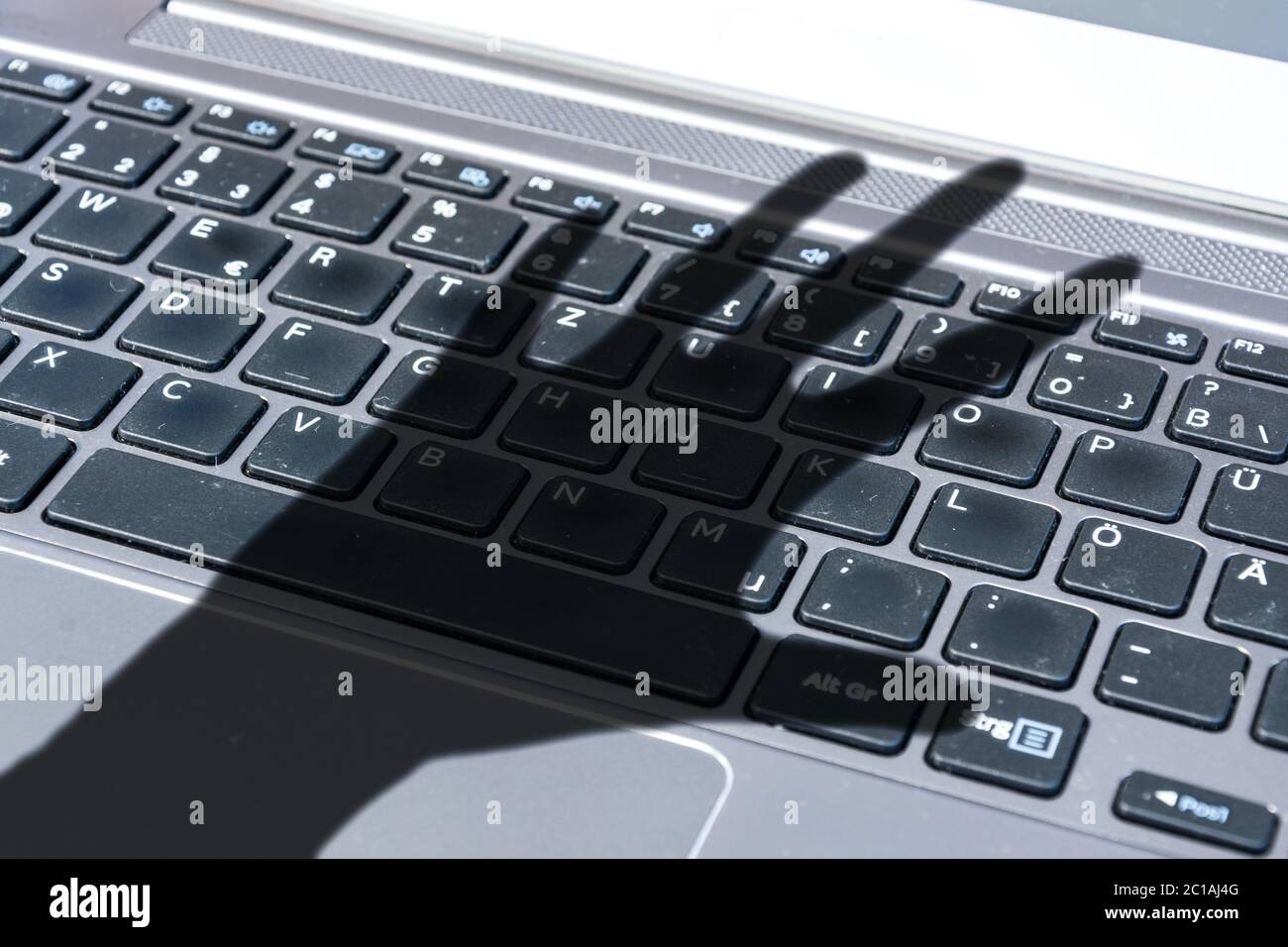 Dark shadow of a hand reaches for computer keyboard symbolizing cyber ...