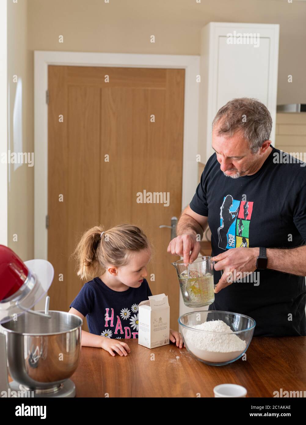 Daddy and daughter making fresh pizza dough in kitchen mixer. Corona ...