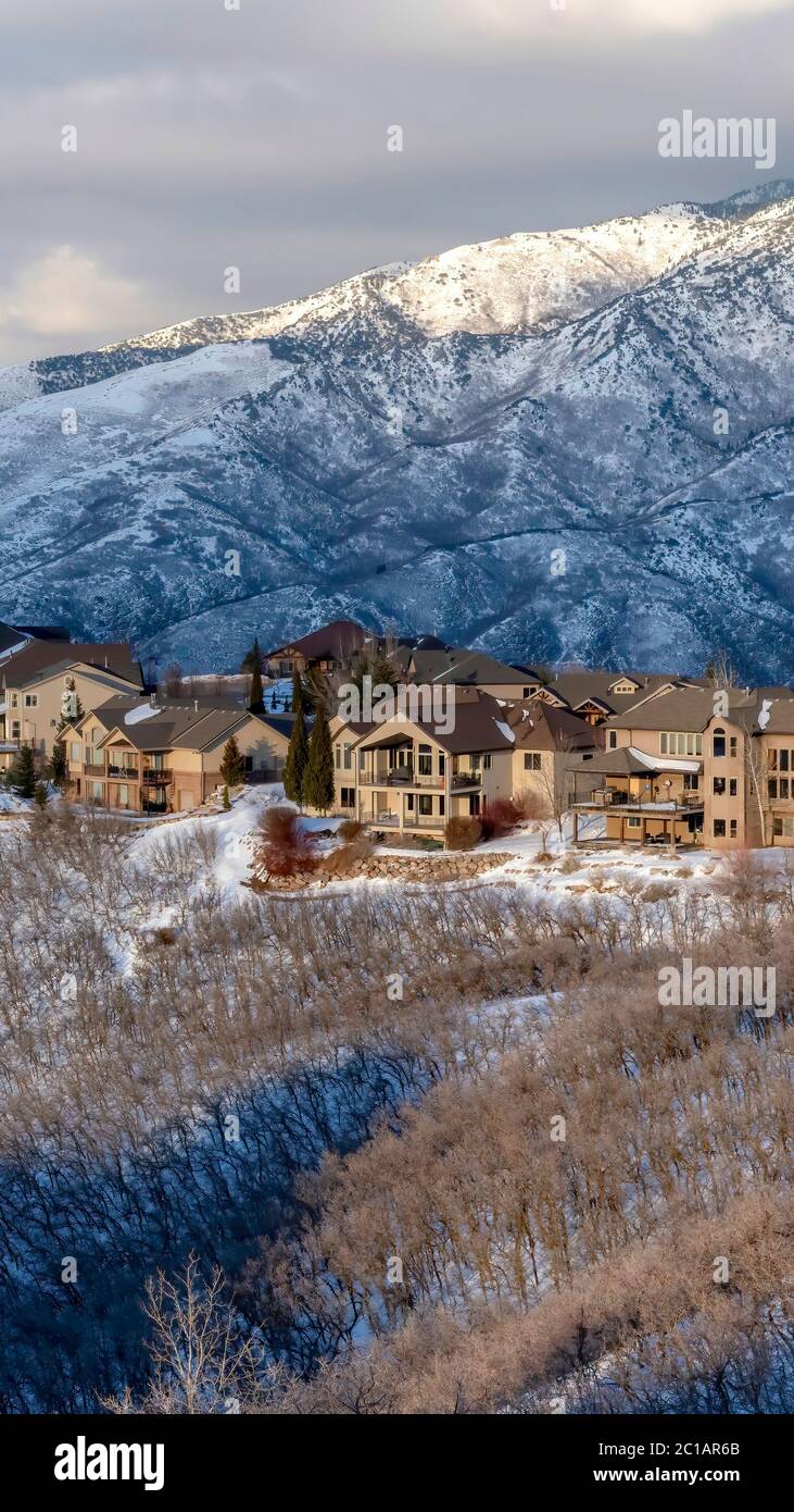 Vertical crop Homes on snowy terrain of Wasatch Mountains with sunlit ...