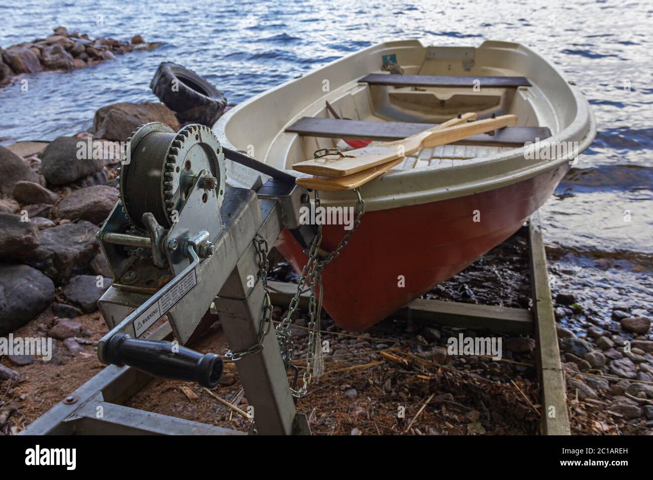 A red rowing boat (oar boat) on a slipway with a winch on lake shore in ...