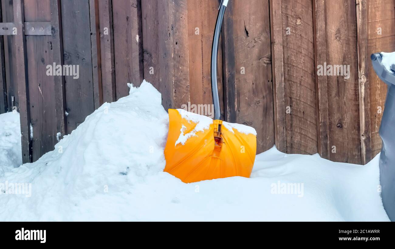 Panorama crop Yelllow snow shovel against snowed in ground and brown ...