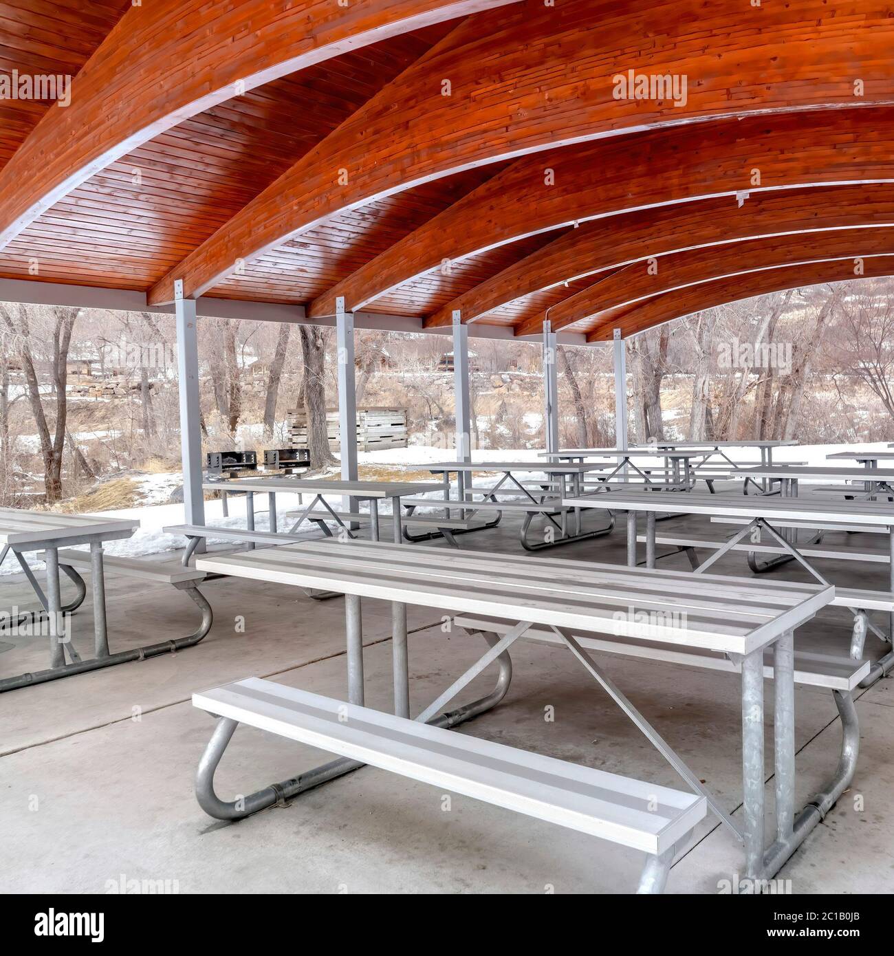 Square Tables and benches inside a park pavilion with wooden arches on ...