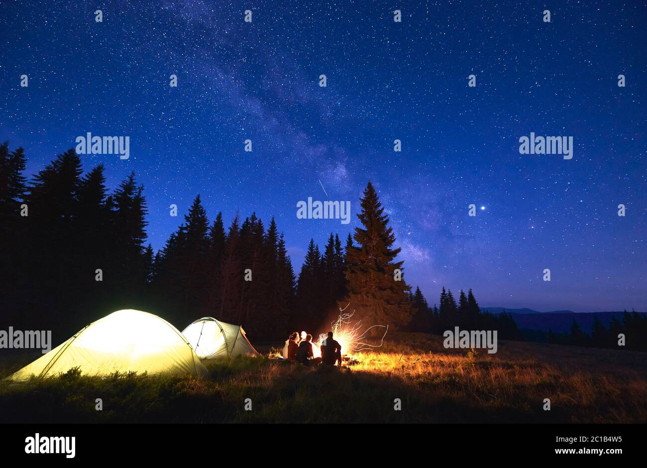 Night camping with bonfire. People bask in campfire near illuminated ...