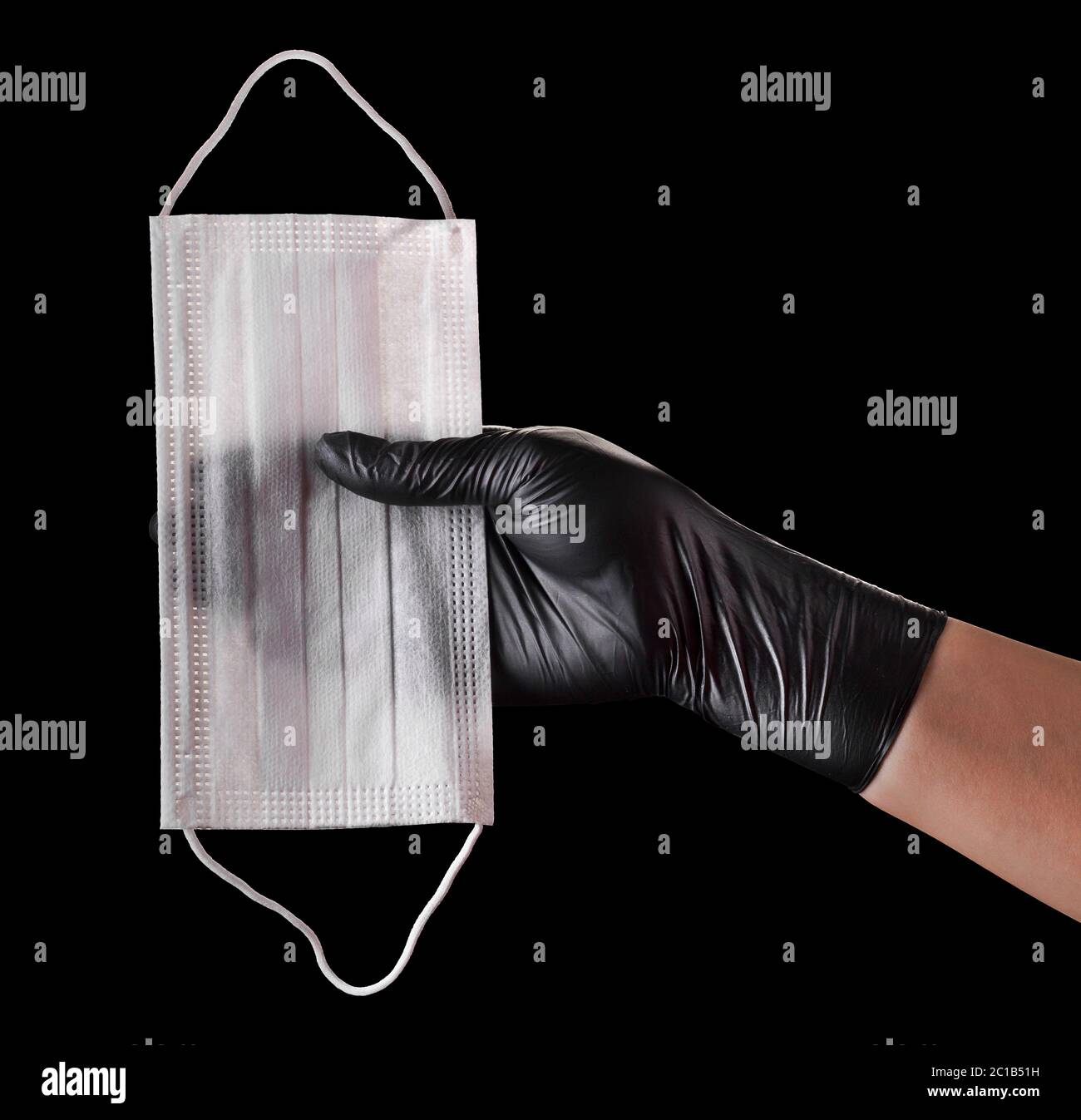 Hand in black gloves holding disposable face mask isolated on black ...