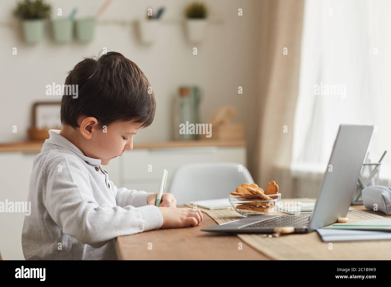 Warm-toned side view portrait of cute boy doing homework while sitting ...
