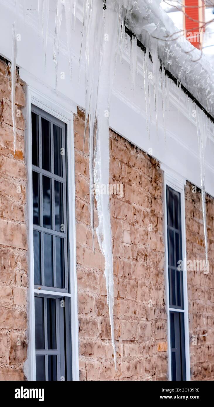 Vertical crop Sharp spiked icicles against windows and stone exterior ...