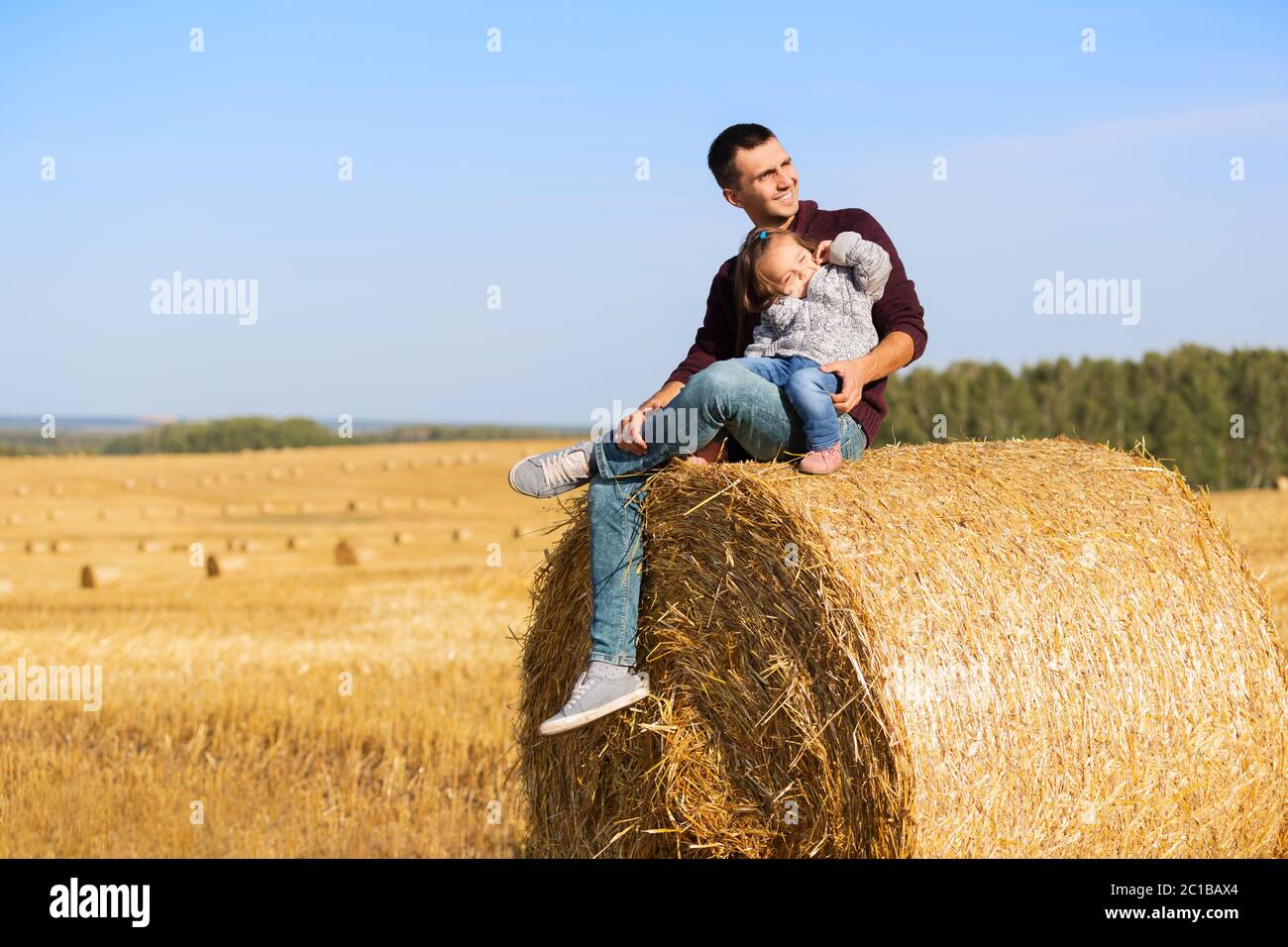 Happy father and two year old girl sitting on hay bale in harvested ...