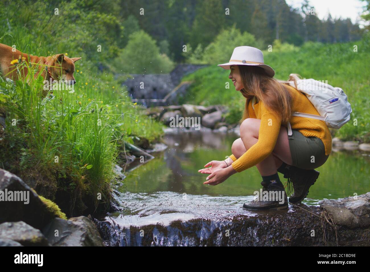 Happy young woman with dog standing by stream on a walk outdoors in ...