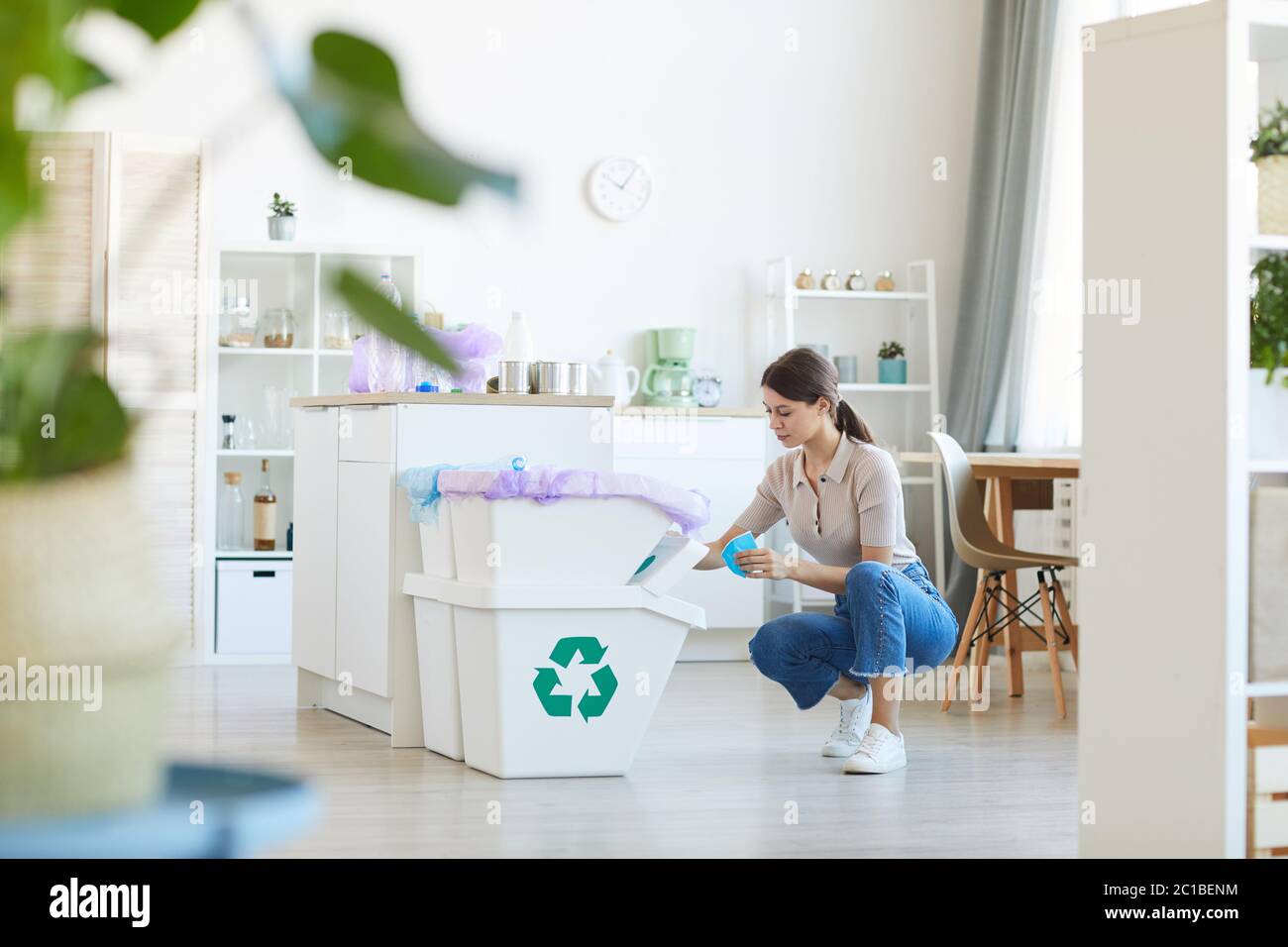 Young woman sorting paper waste into the bins in the domestic kitchen ...
