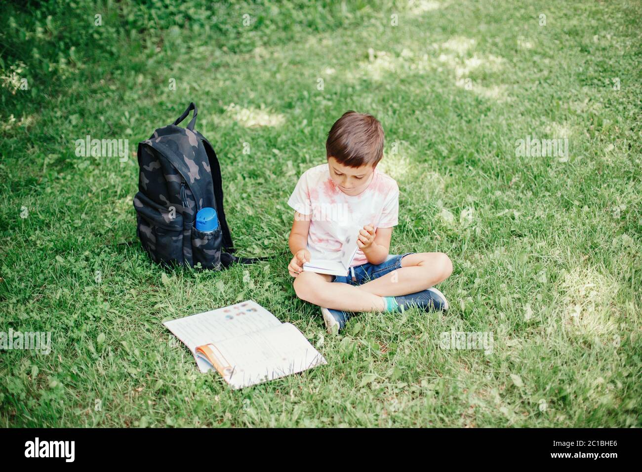Young Caucasian school boy sitting in park outdoor doing school ...